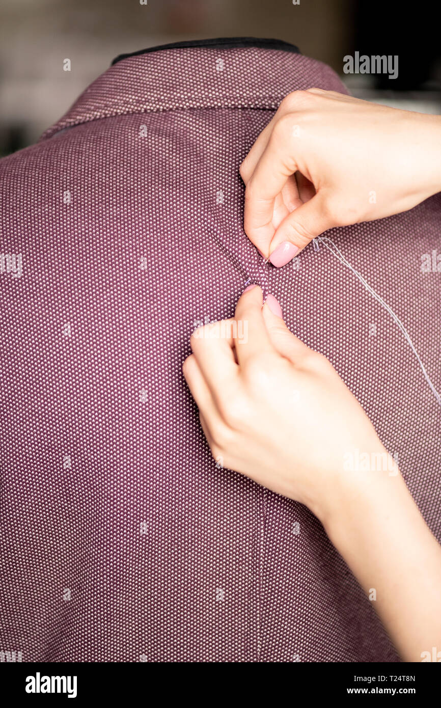 Hands of young seamstress with needle and white thread sewing back of ...