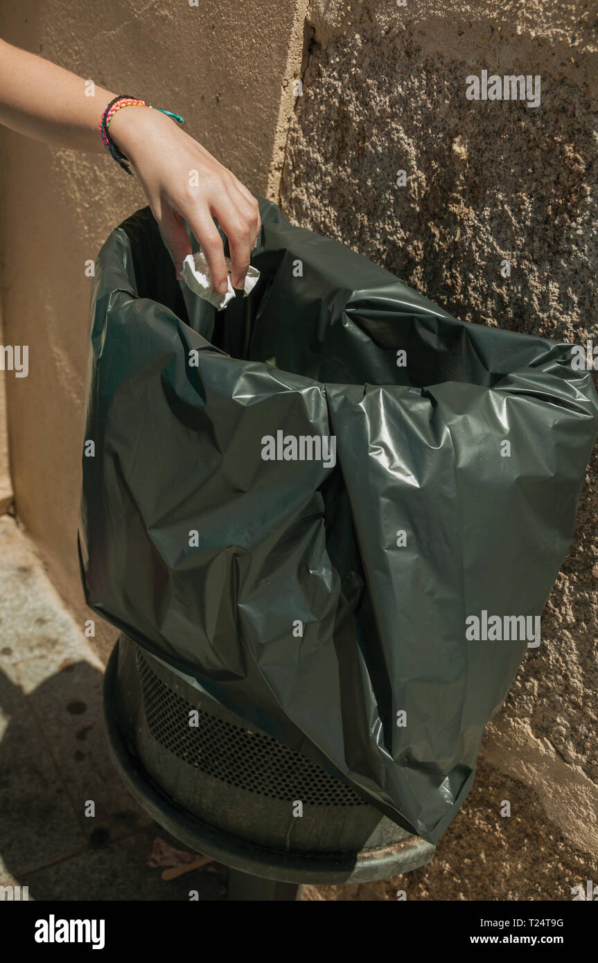 Hand of girl throwing waste in a trash can next to a wall, in a sunny ...