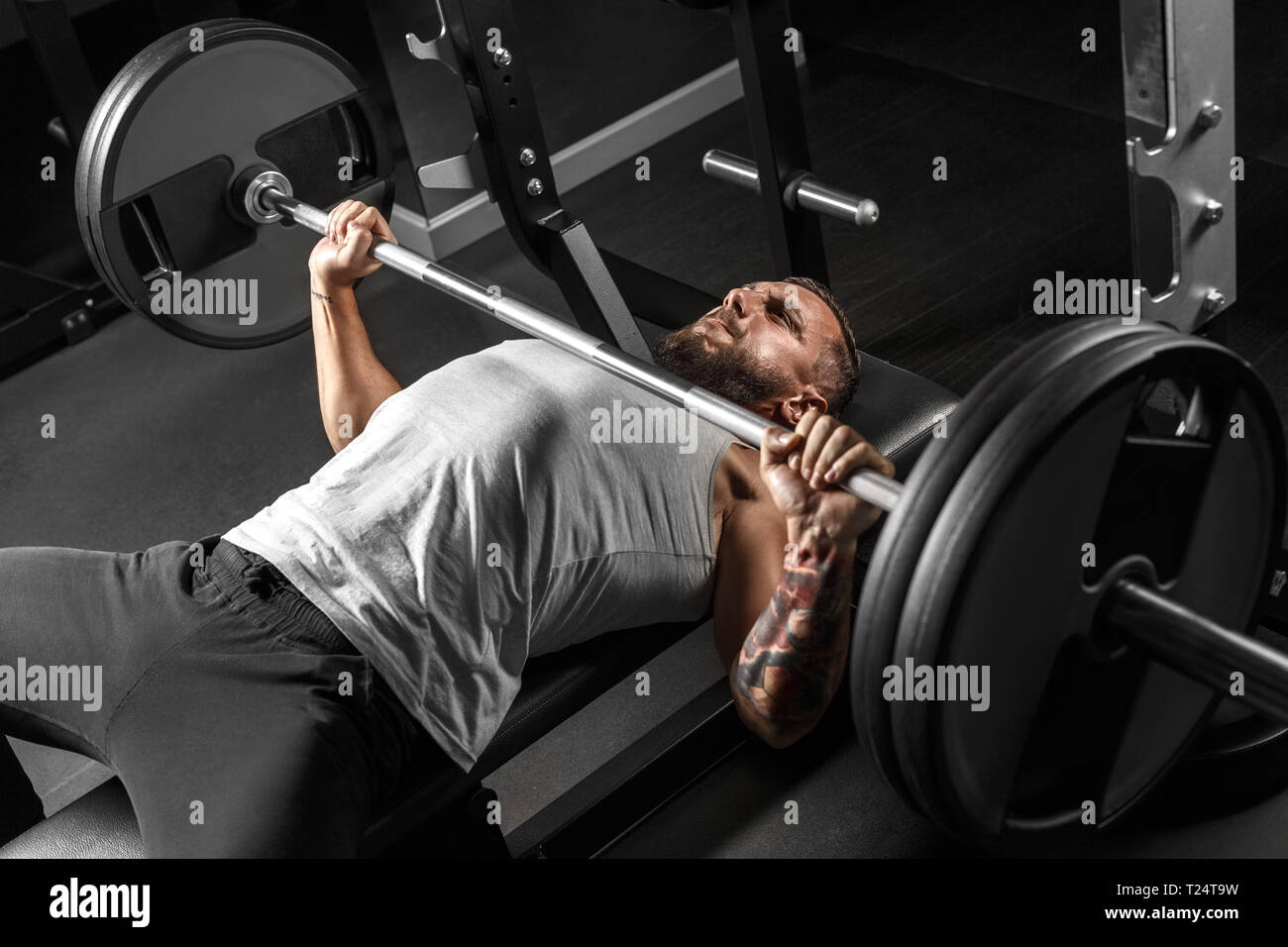 Bearded man bodybuilder exercising at gym lying doing bench press ...