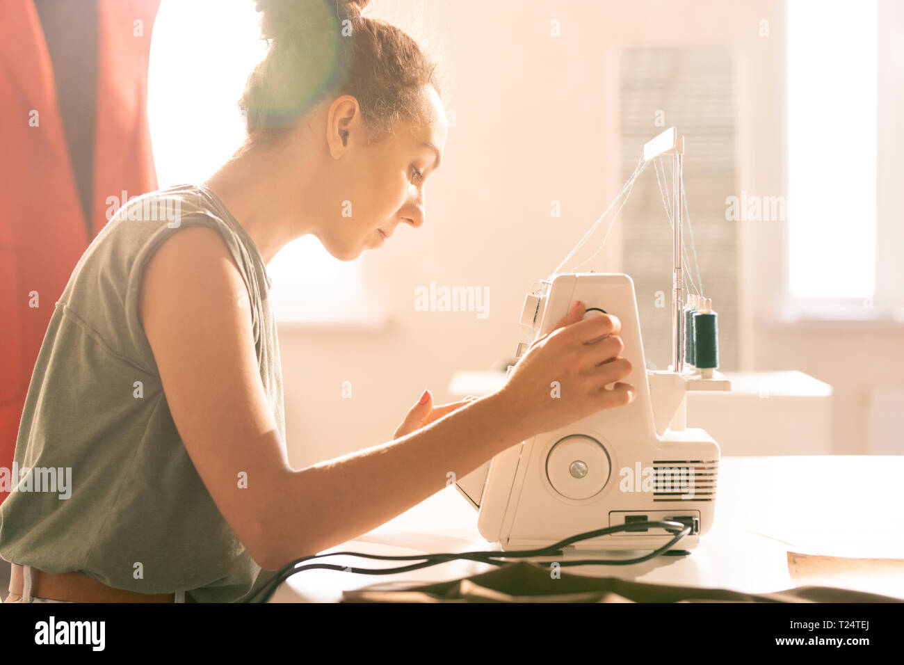Young seamstress bending over sewing machine while sitting by workplace ...