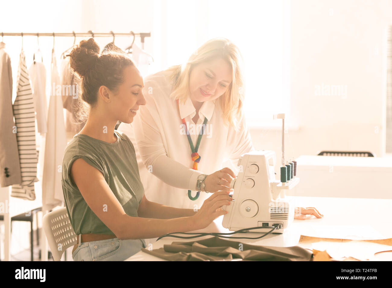 One of colleagues helping young seamstress with sewing machine before ...