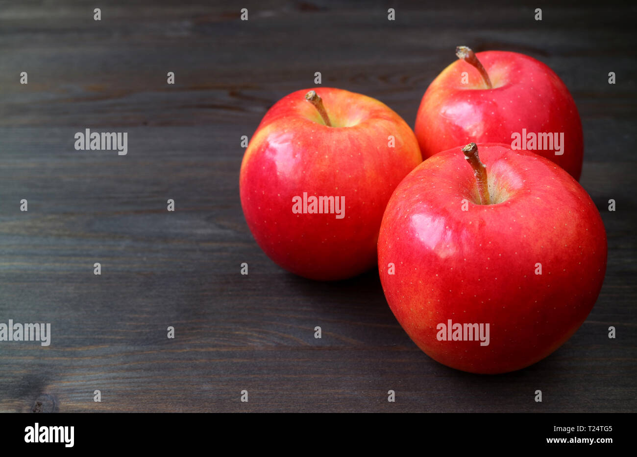Three red apples on dark colored wooden table with free space for text ...