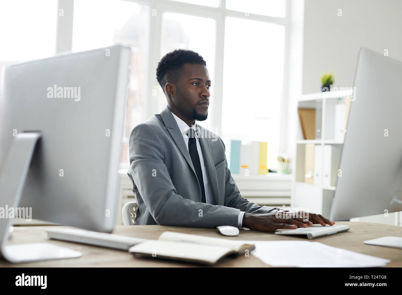 Young elegant man in formalwear looking at screen of one of computers ...