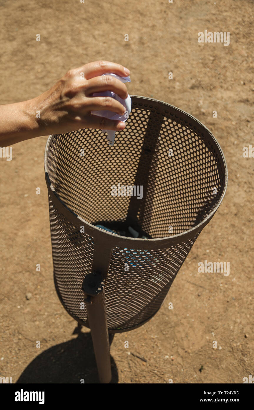 Hand of woman throwing waste inside a trash can in a park, in a sunny ...