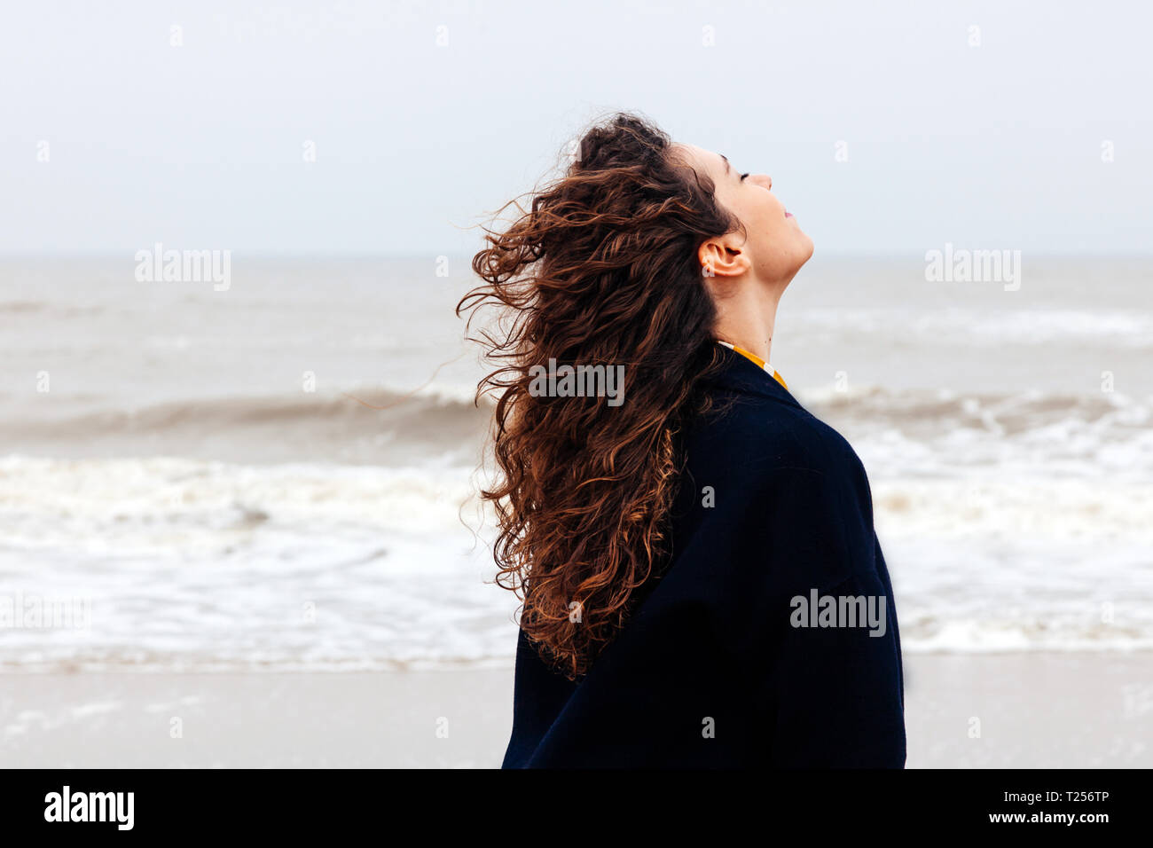 Close-up of a girl with long curly hair against a cold winter sea ...