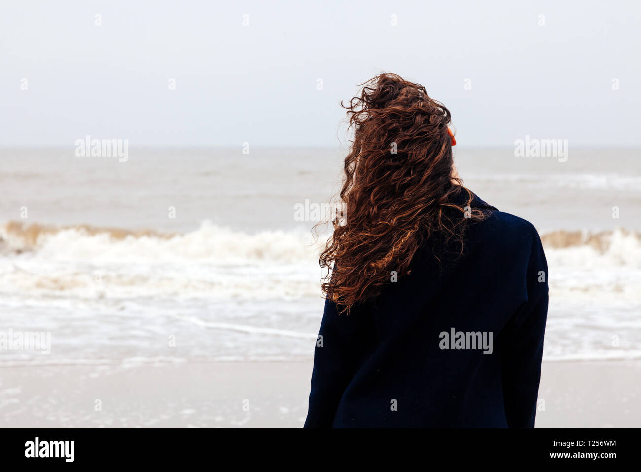Close-up of a girl with long curly hair against a cold winter sea ...