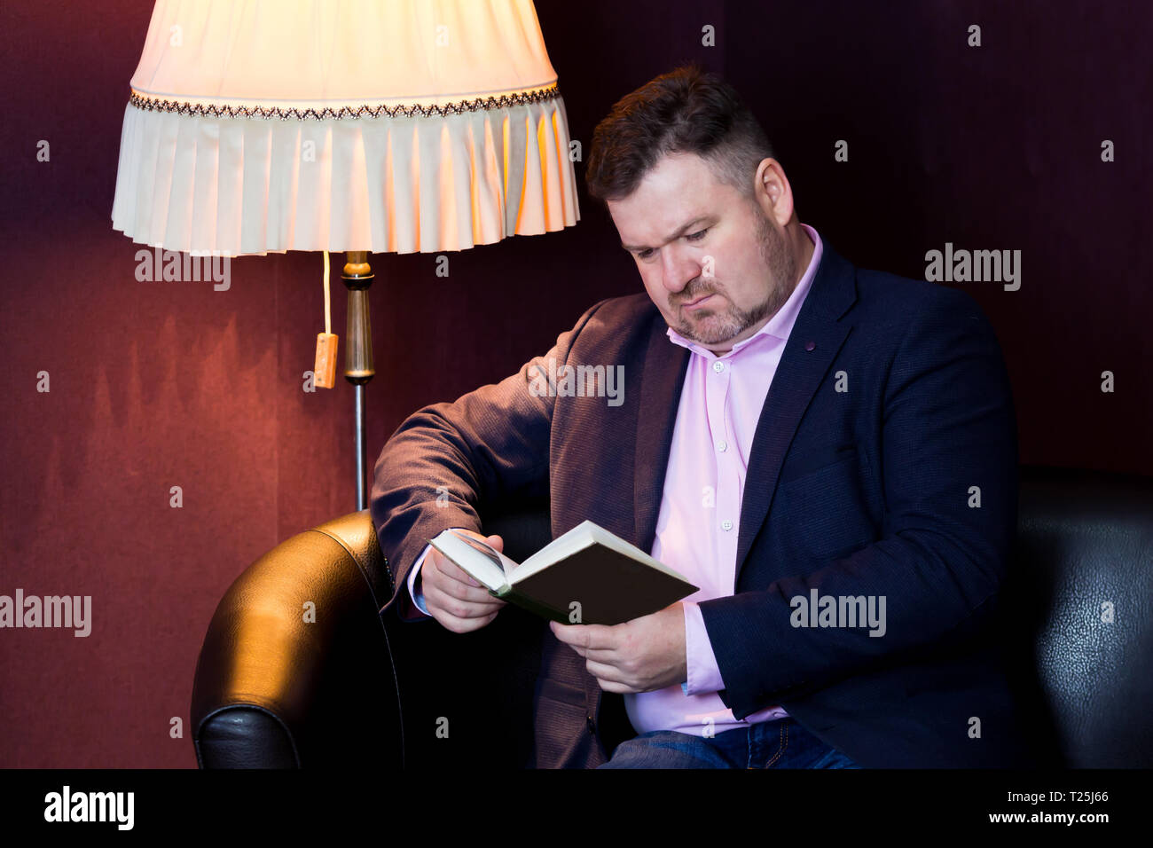 A fat man with a beard is sitting on the couch and reading a book Stock ...