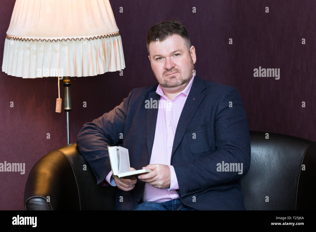 A fat man with a beard is sitting on the couch and reading a book Stock ...
