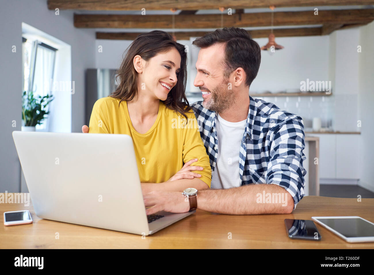 Couple sitting at dining table, using laptop, smiling Stock Photo - Alamy