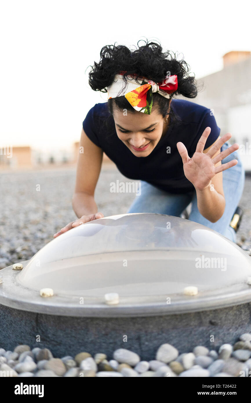 Smiling young woman looking through skylight on roof terrace raising ...