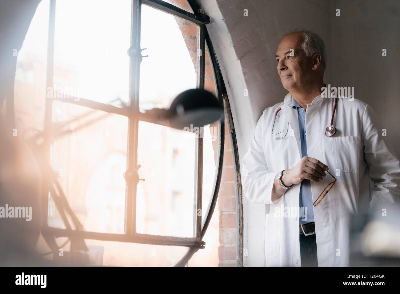 Senior doctor looking out of window in medical practice Stock Photo - Alamy