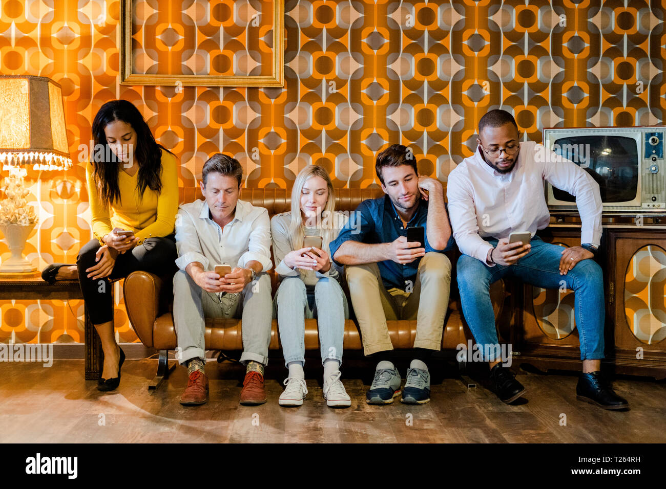 Group of people sitting on couch in vintage living room using cell ...
