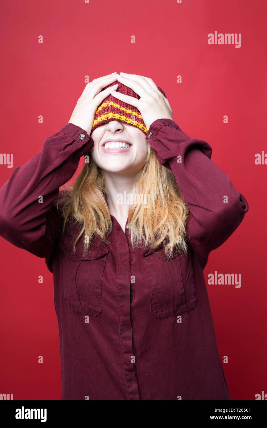 Grinning young woman wearing wooly hat in front of red background Stock ...