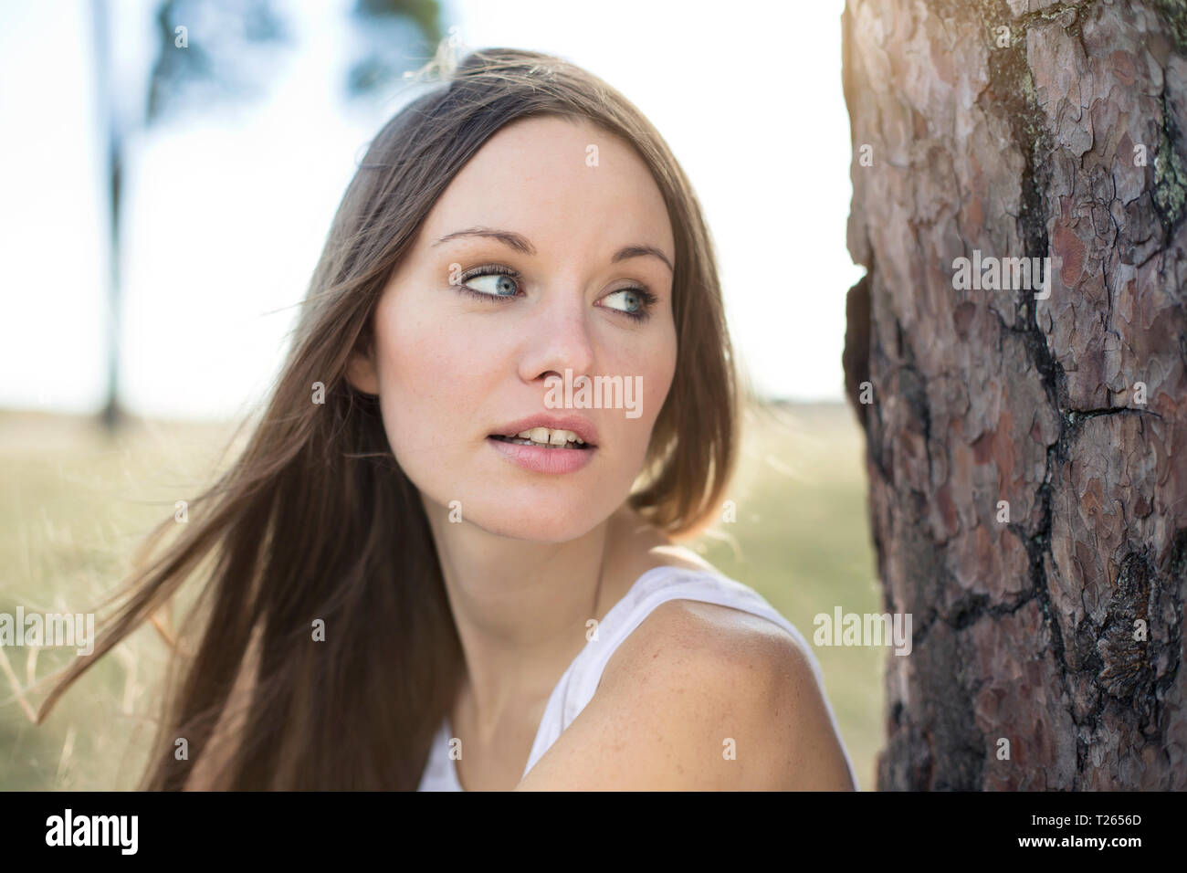 Portrait of young woman leaning against tree trunk Stock Photo - Alamy