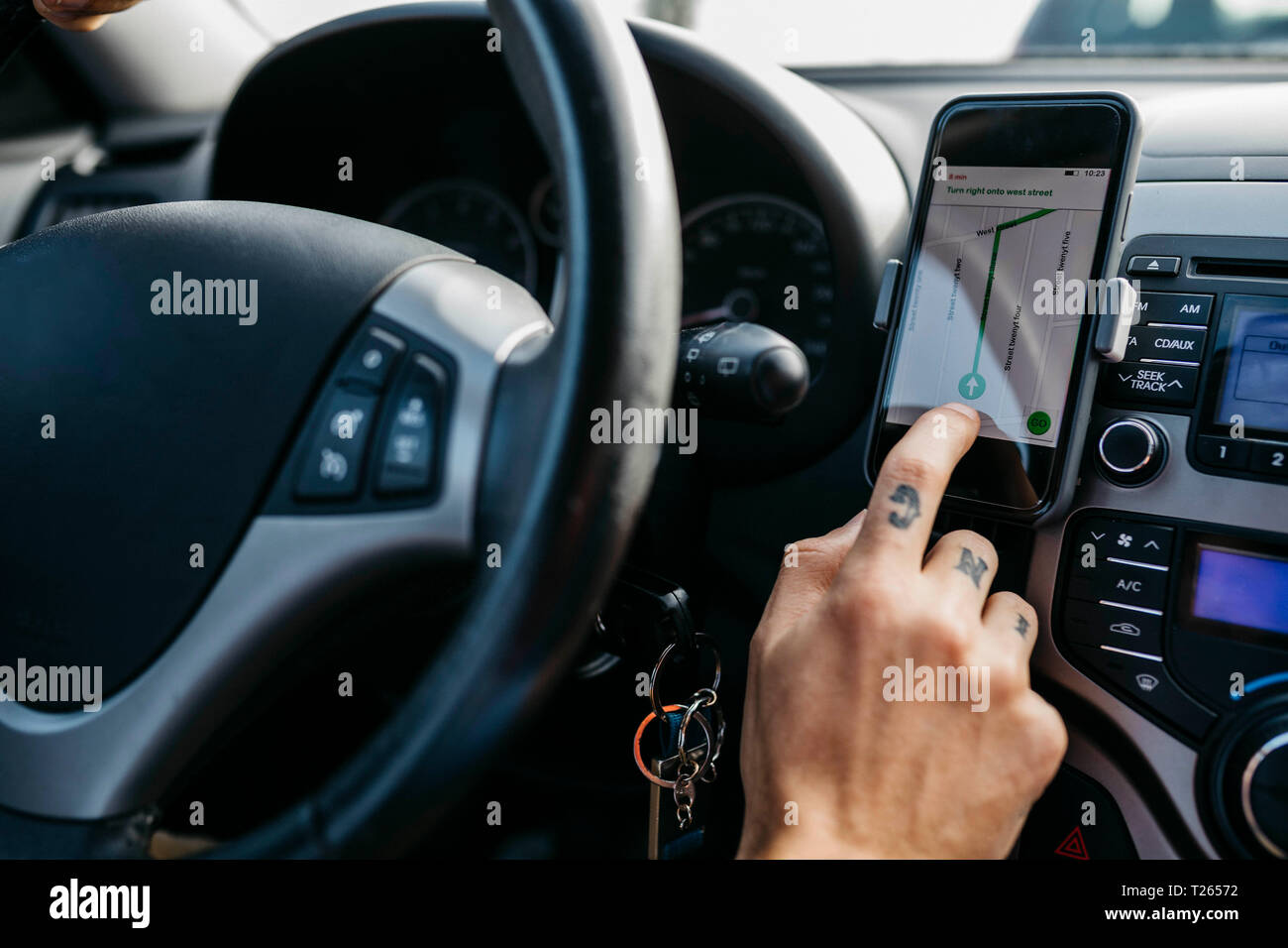 Close-up of man with tattooed hand driving car using cell phone as ...