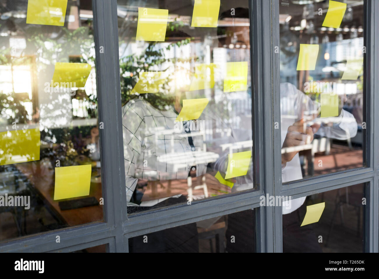 Businessman with colleague brainstorming with post-its on window front ...