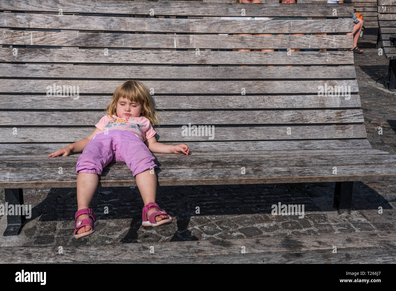 Sweden, girl lying on wooden bench on town square Stock Photo - Alamy