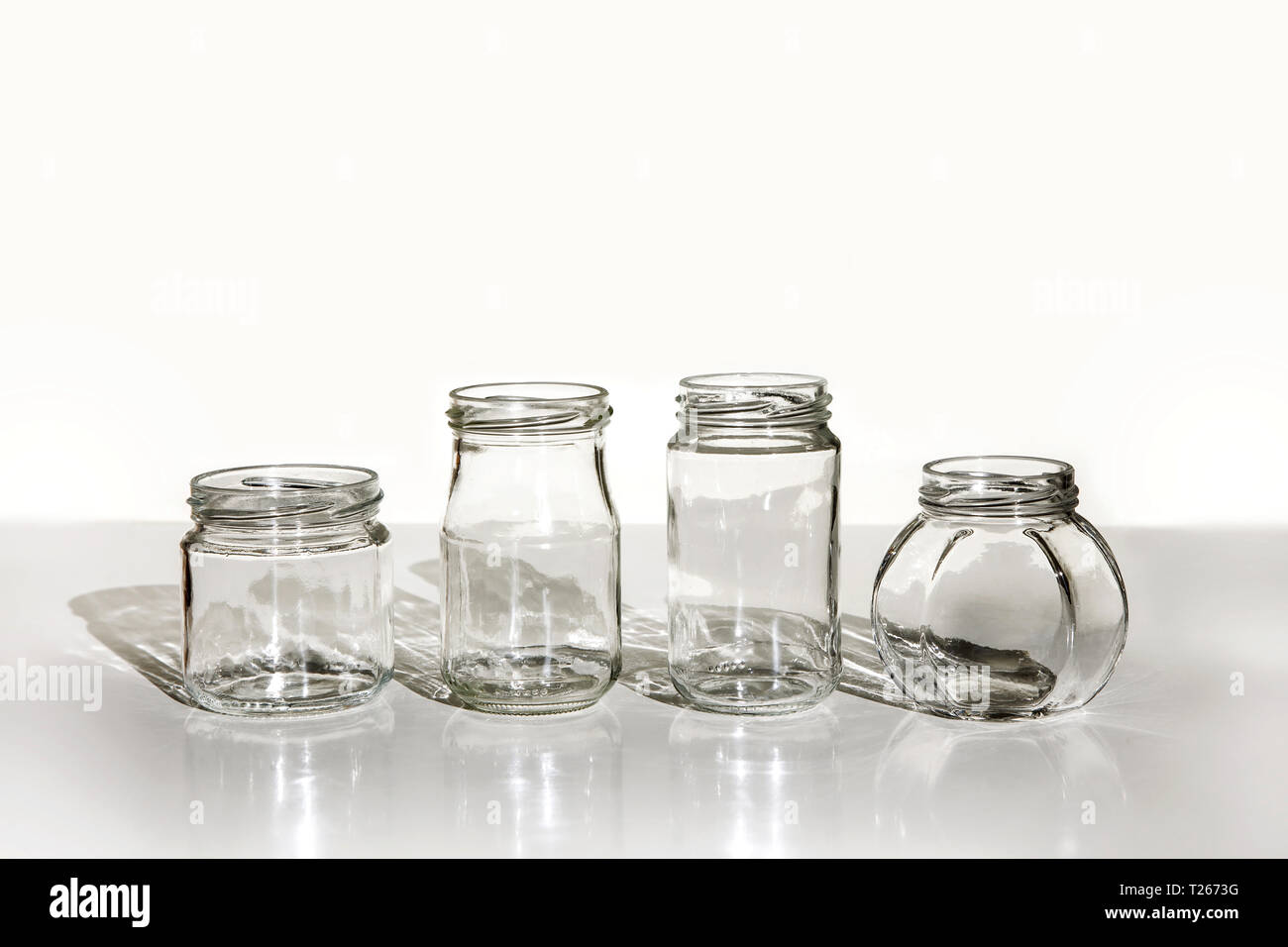 Four clean glass jars on white table with shadow. Set of empty jars ...