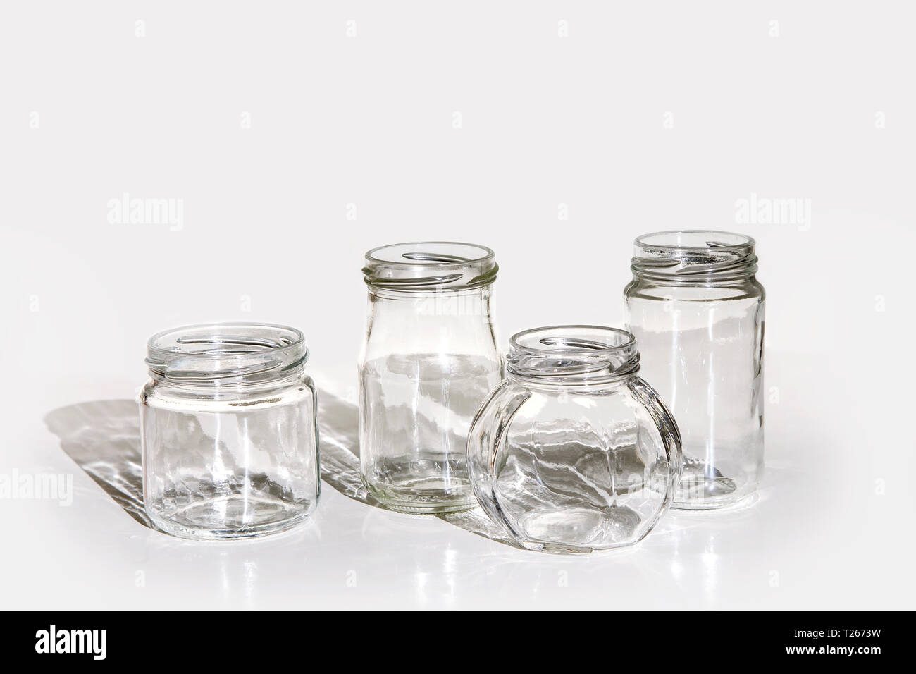 Four clean glass jars on white table with shadow. Set of empty jars ...
