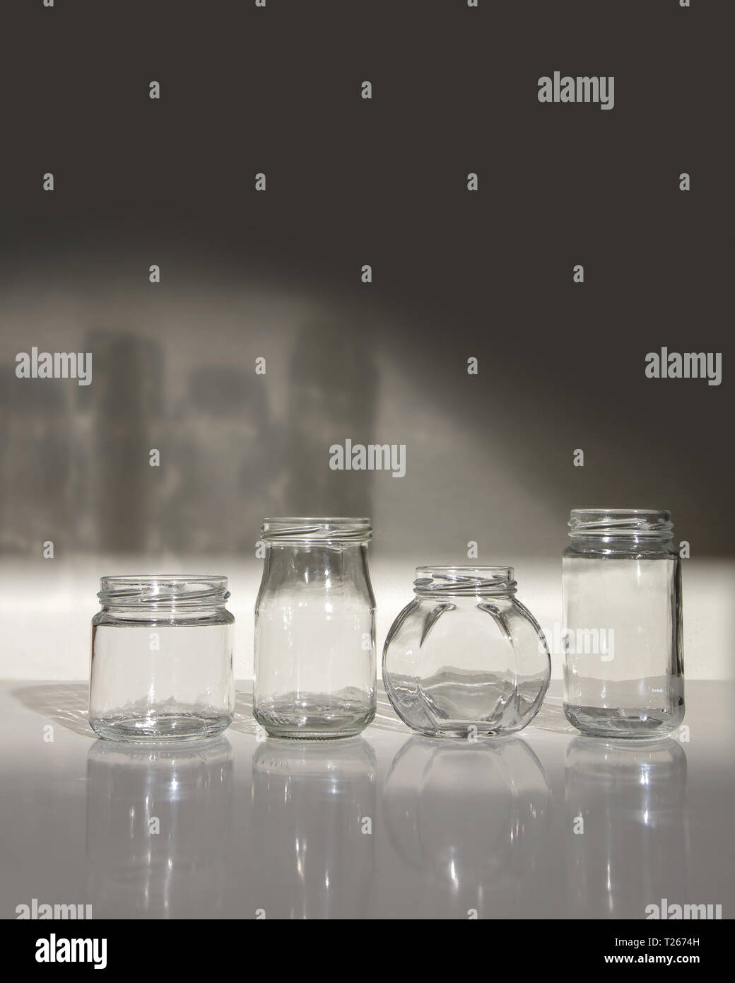 Four clean glass jars on white table with shadow. Set of empty jars ...