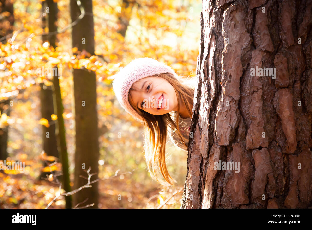 Young girl behind tree in autumn Stock Photo - Alamy