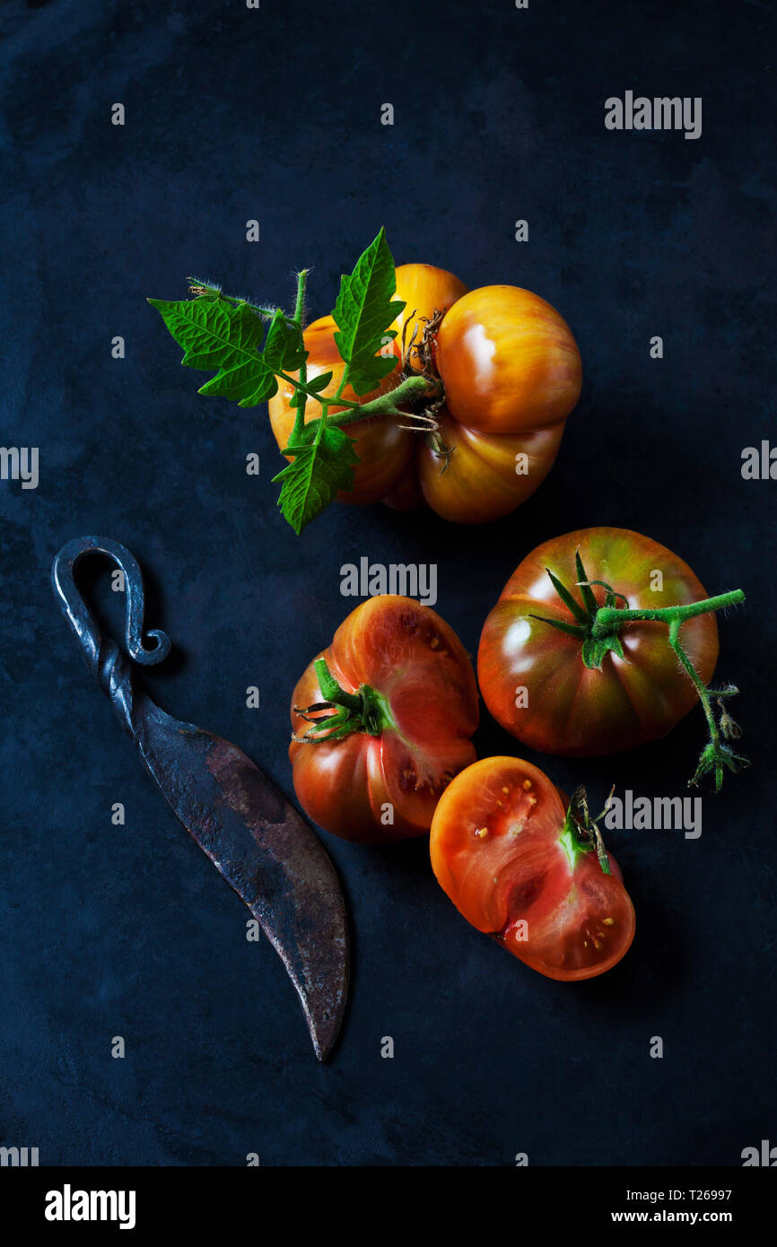 Whole and sliced beef tomatoes 'Chocolate Stripes' and knife on dark ...