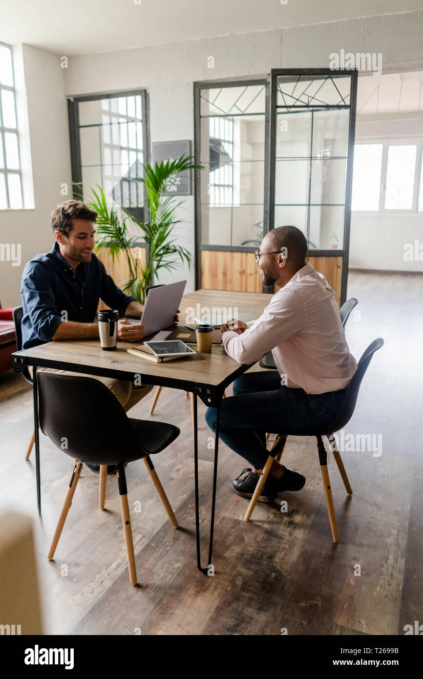Two young businessmen talking at conference table in loft office Stock ...