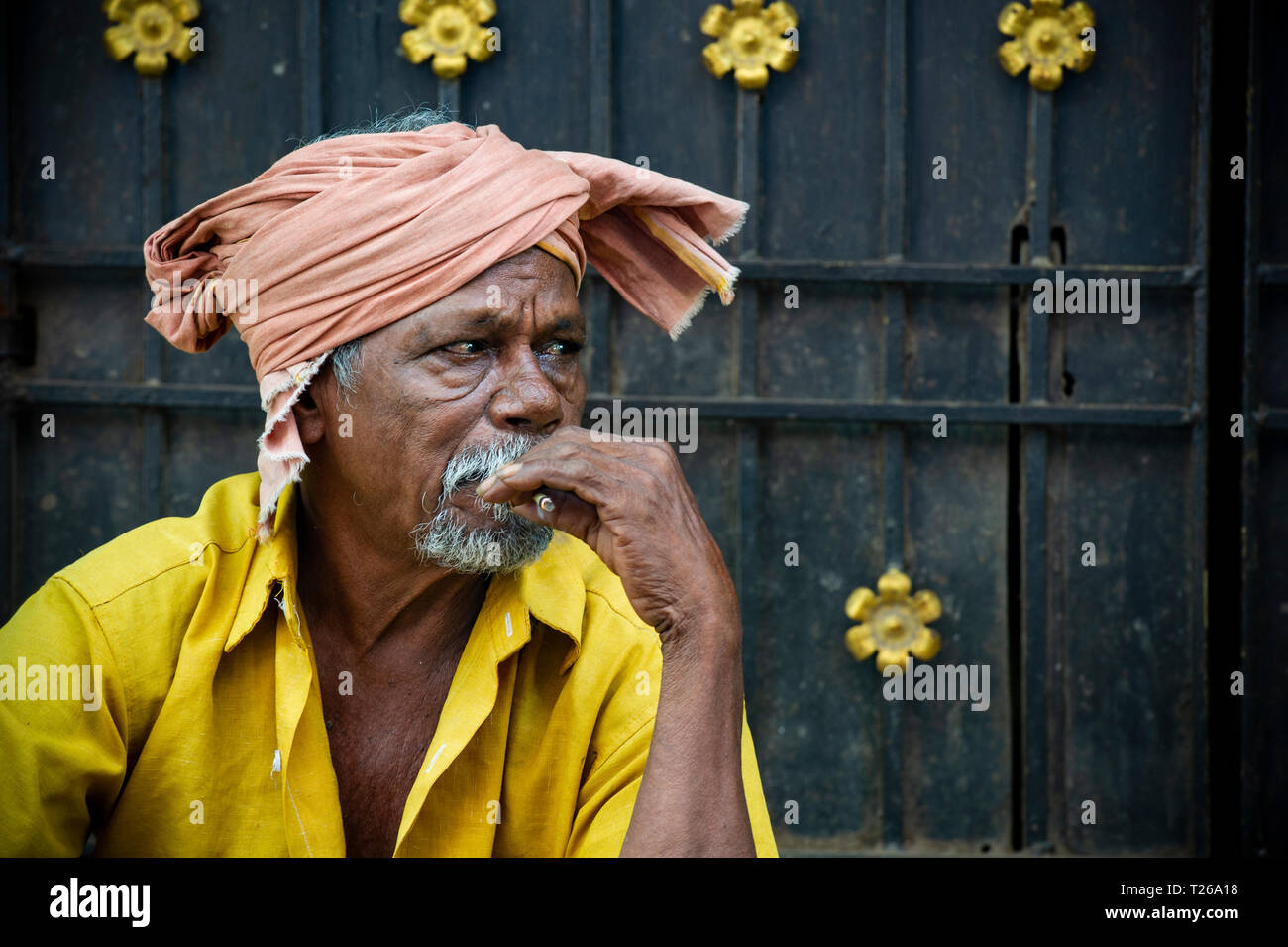 A wise looking man with a turban style hat smokes a cigarette and ...