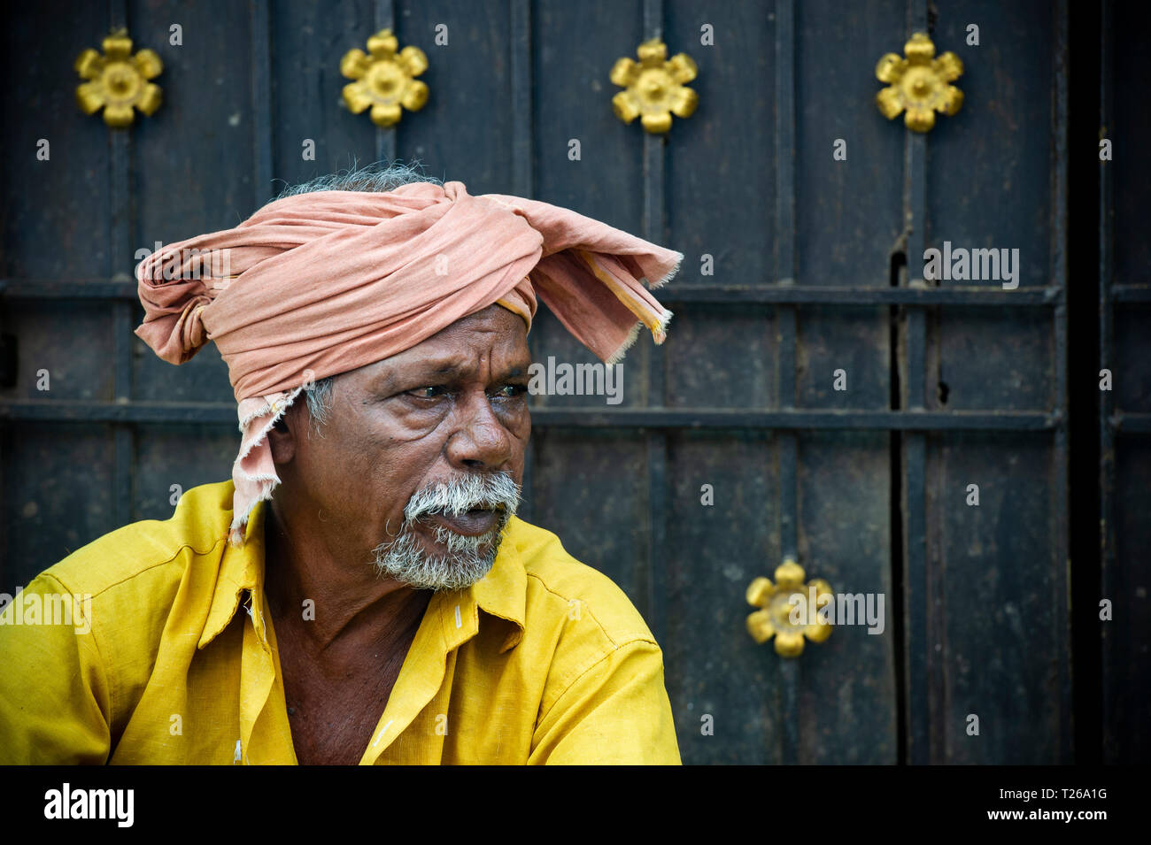 A wise looking man with a turban style hat smokes a cigarette and ...