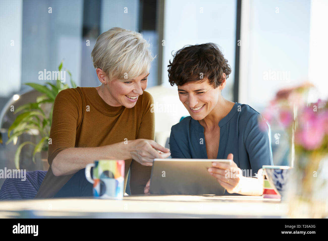 Two happy women sharing tablet at table Stock Photo - Alamy