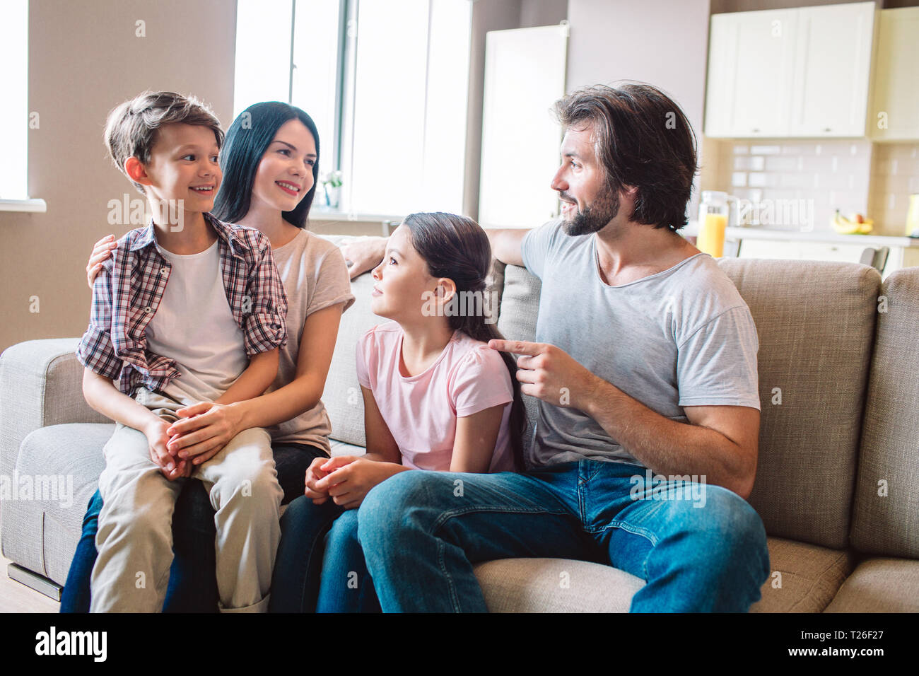 Happy family sits together on sofa. Boy is on mother's lap. Girl sits ...