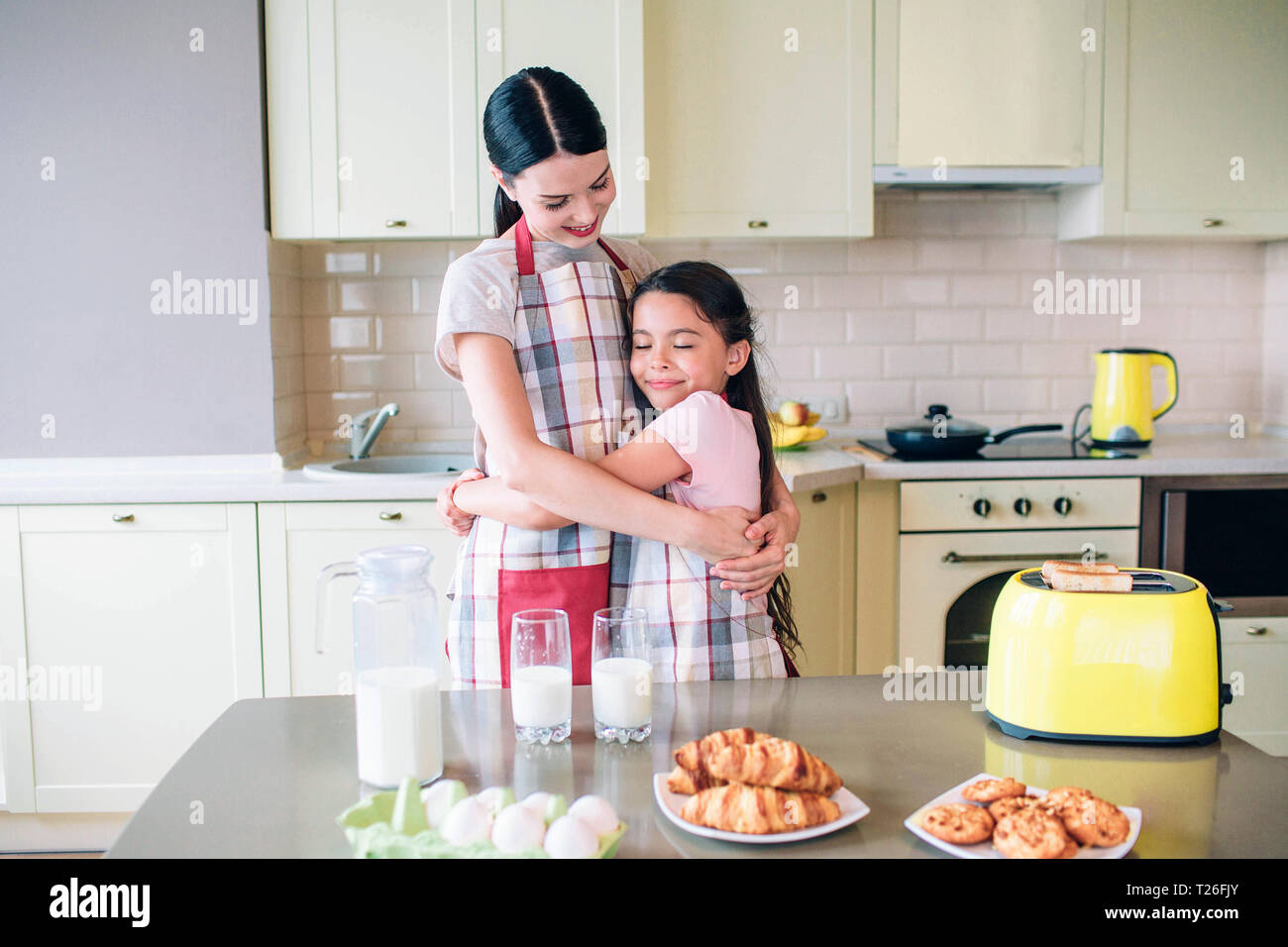 Happy girls are standing togehter at kitchen and smiling. They hug each ...