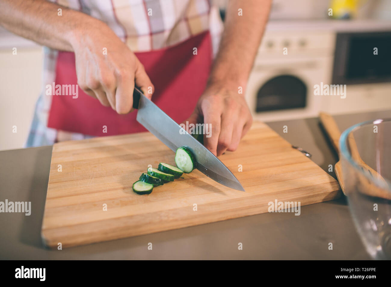 Close up of man's hands holding knife and cutting cucumber into pieces ...