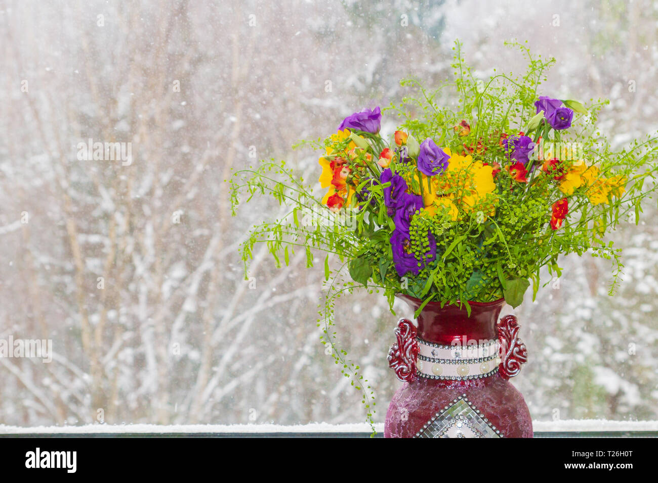 A beautiful vase of spring flowers stands on a window in a snowstorm ...