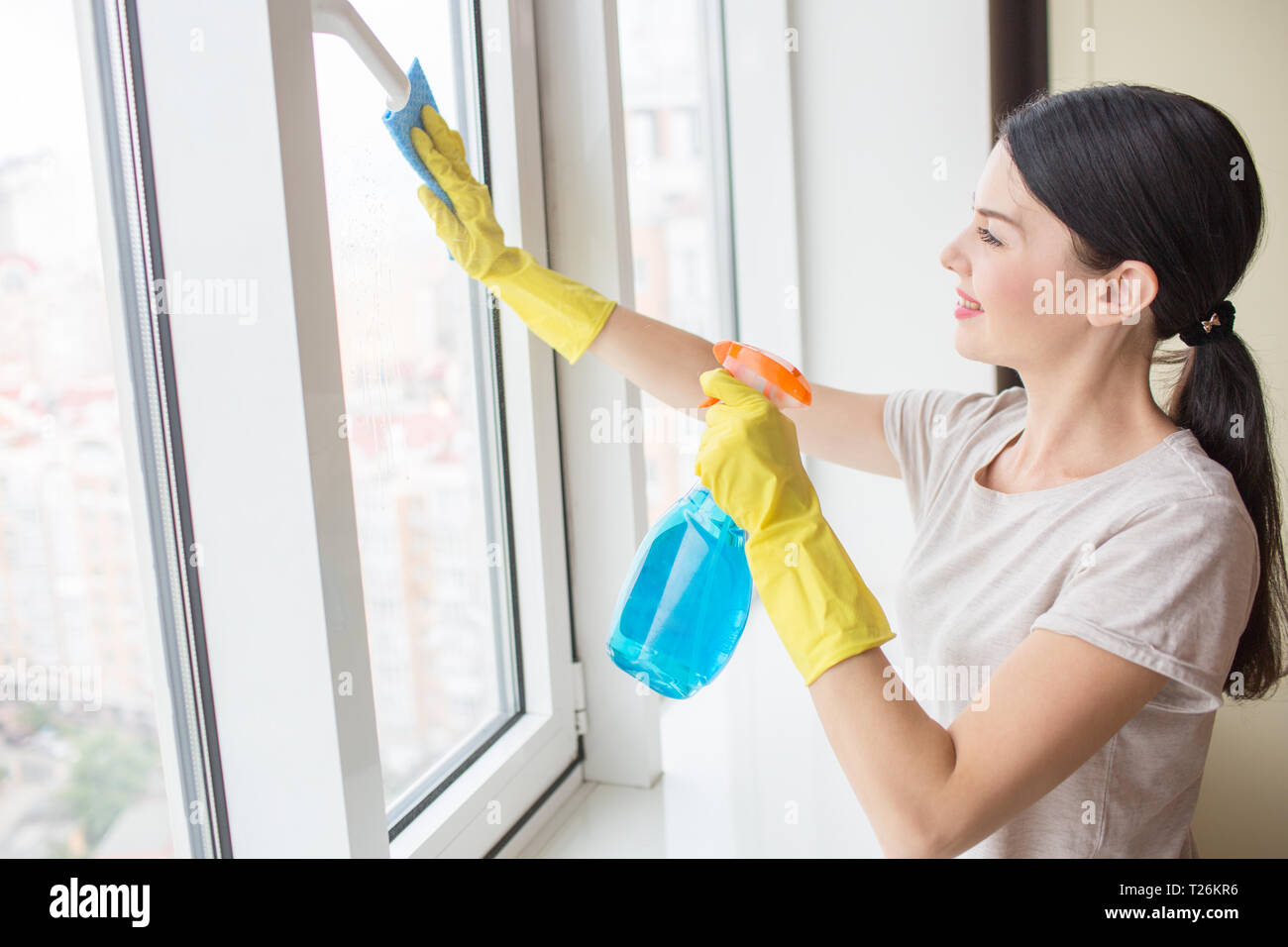 Nice and delightful girl stands in front of window and cleaning it with ...