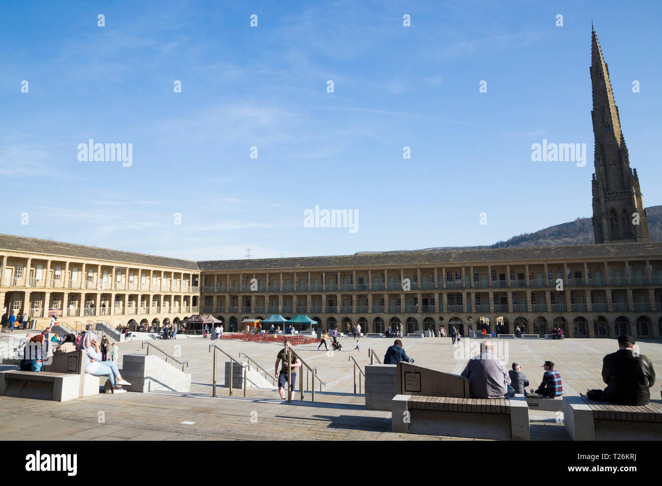 Visitors relax in The Piece Hall with Square Chapel church spire behind ...