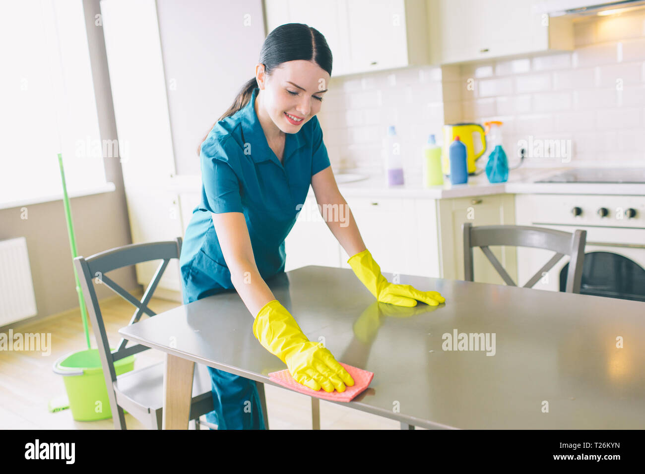 Positive female cleaner looks down and leans to table. She cleans it ...