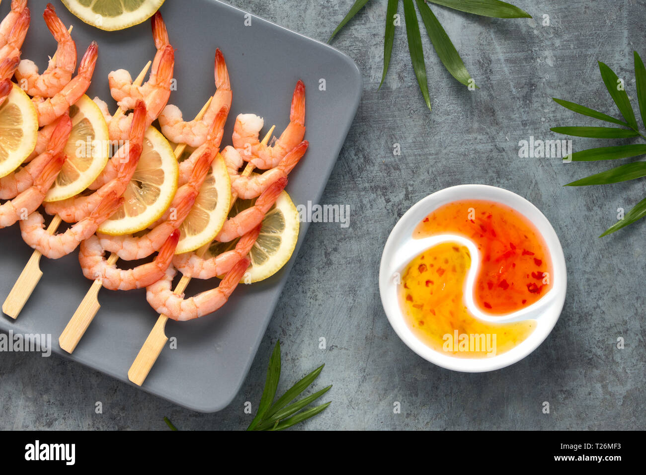 Zesty lemon and garlic prawns on wooden sticks, flat lay on dark ...