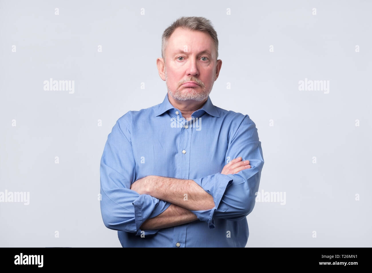 Serious senior man in blue shirt with folded arms and a deadpan ...