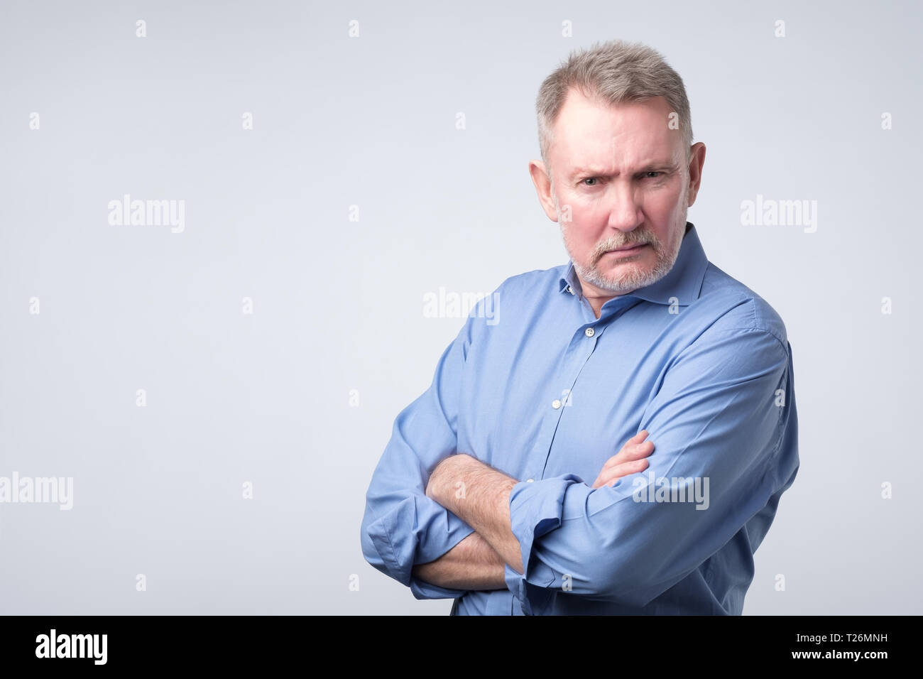 Serious senior man in blue shirt with folded arms and a deadpan ...