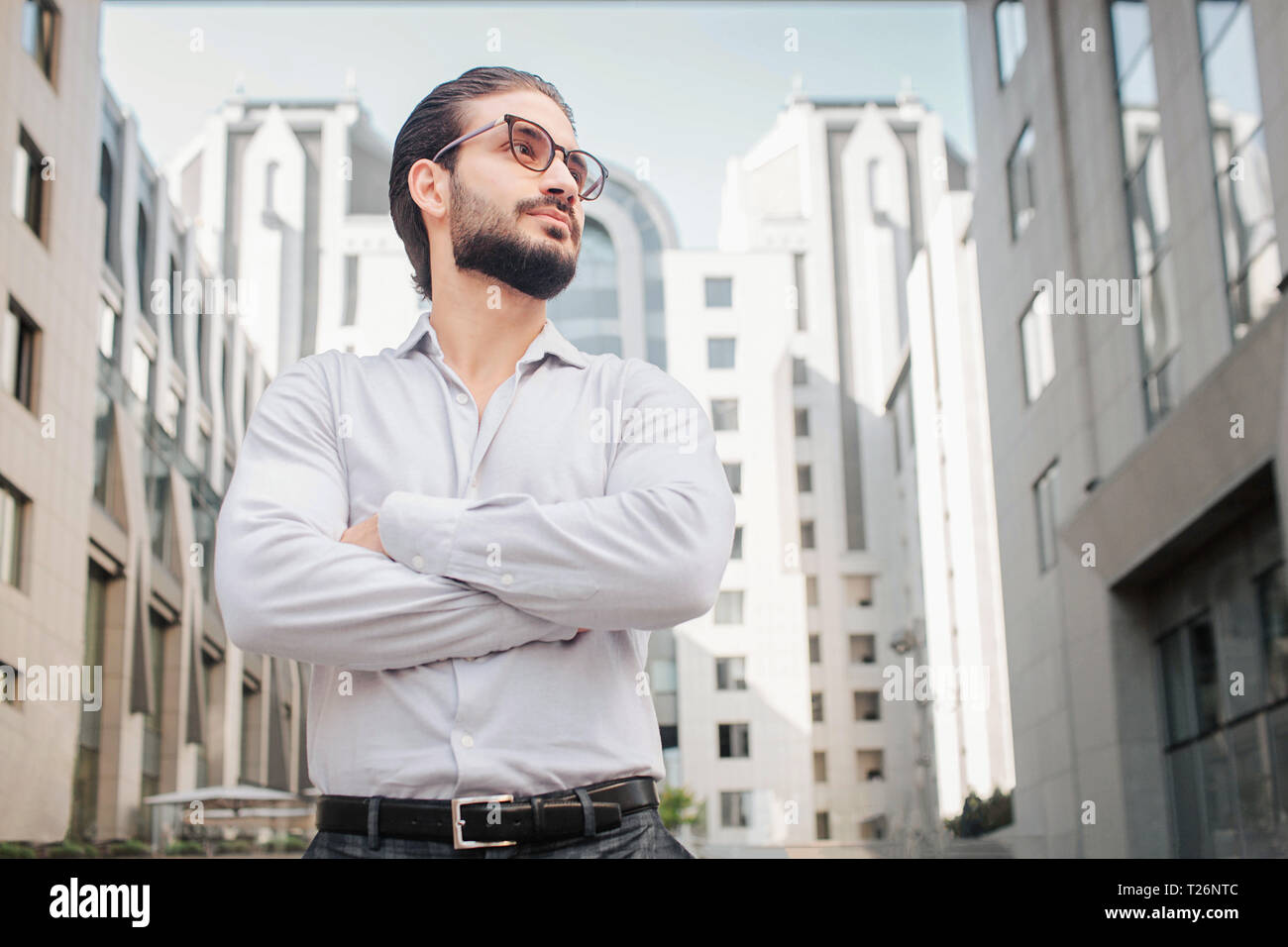 Serious young man stand and pose. He keeps hands crossed and looks ...
