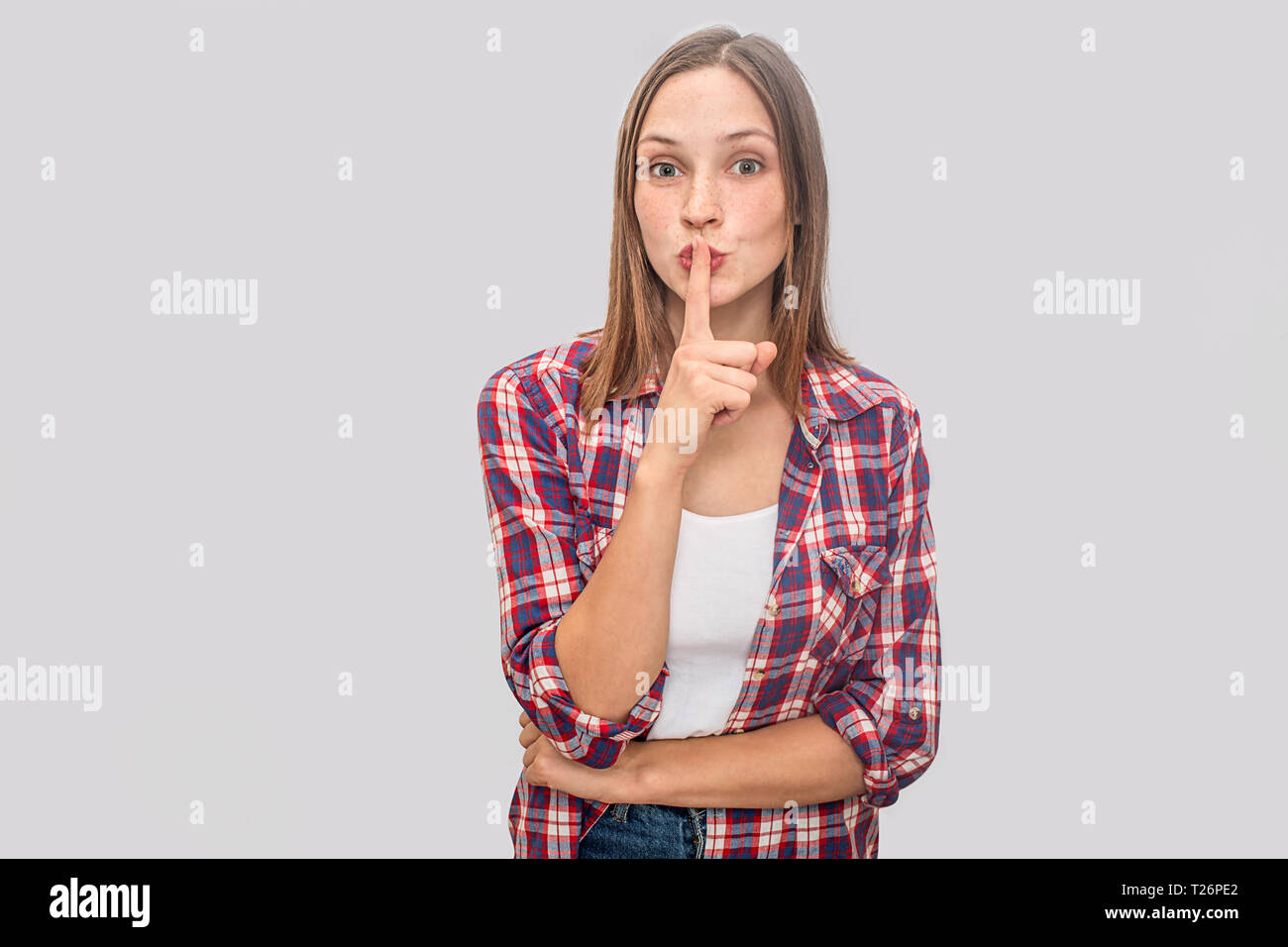 Serious young woman keeps finger on lips. Another hand is on hips. She ...