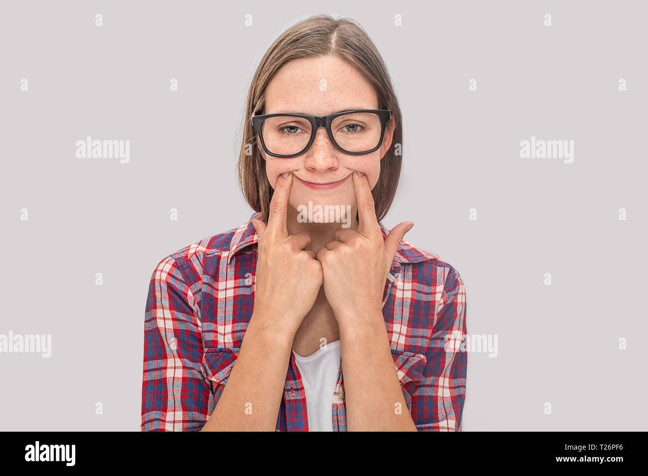 Bored but funny young woman puts fingers on her smiles. She looks ...