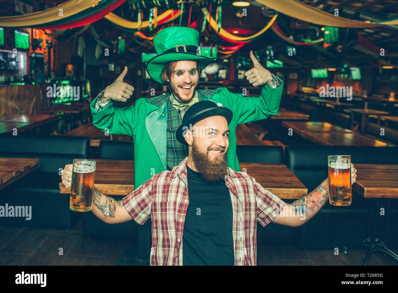 Happy friends stand in pub and pose on camera. They look straight. Guy ...