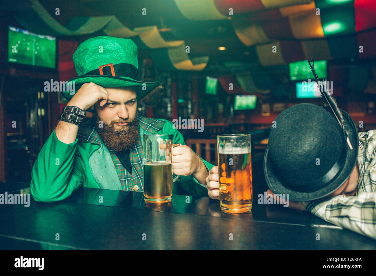 Drunk young man in green suit sit at bar counter in pub with friend ...