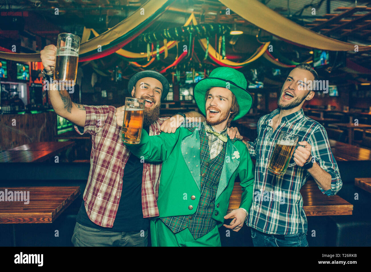 Happy three young men singing and waving with beer mugs in pub. They ...