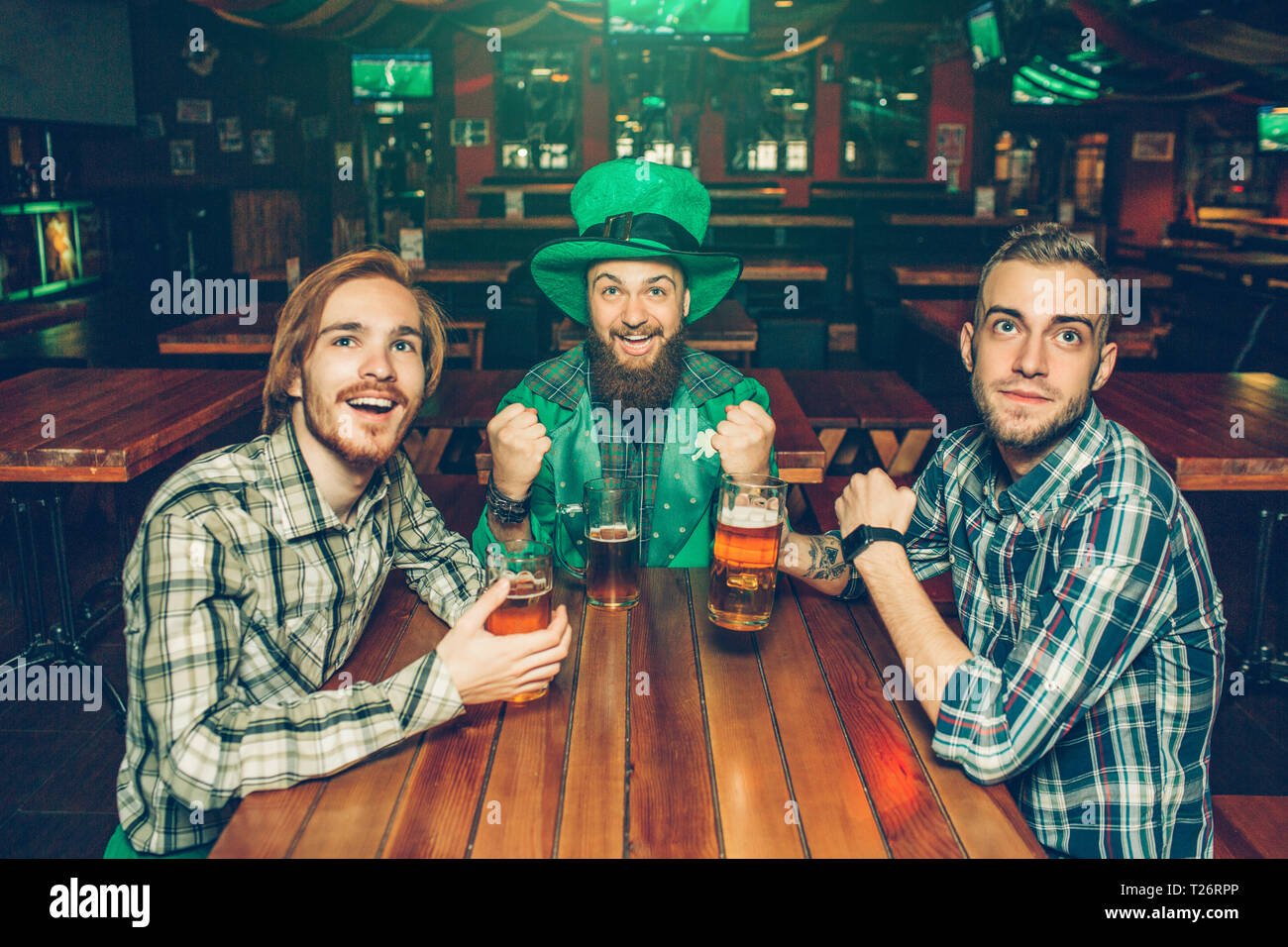 Three young excited men cheering at table in pub. They look up forward ...