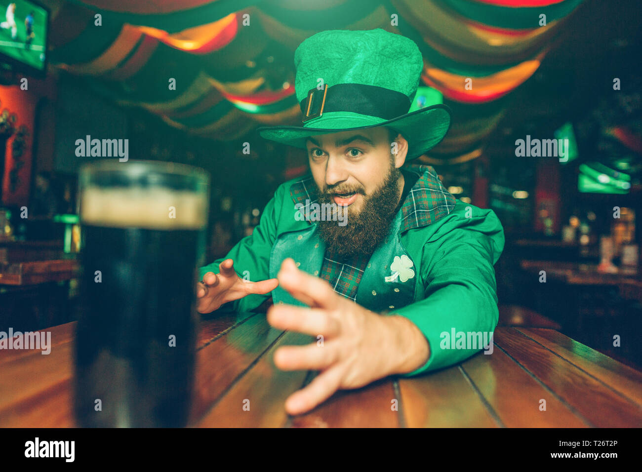Afraid bearded guy in green suit sit at table in pub. He reach mug of ...