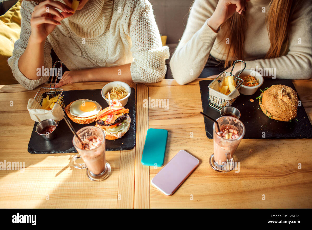 Cut view of table full of food and drink. There are young women sit at ...