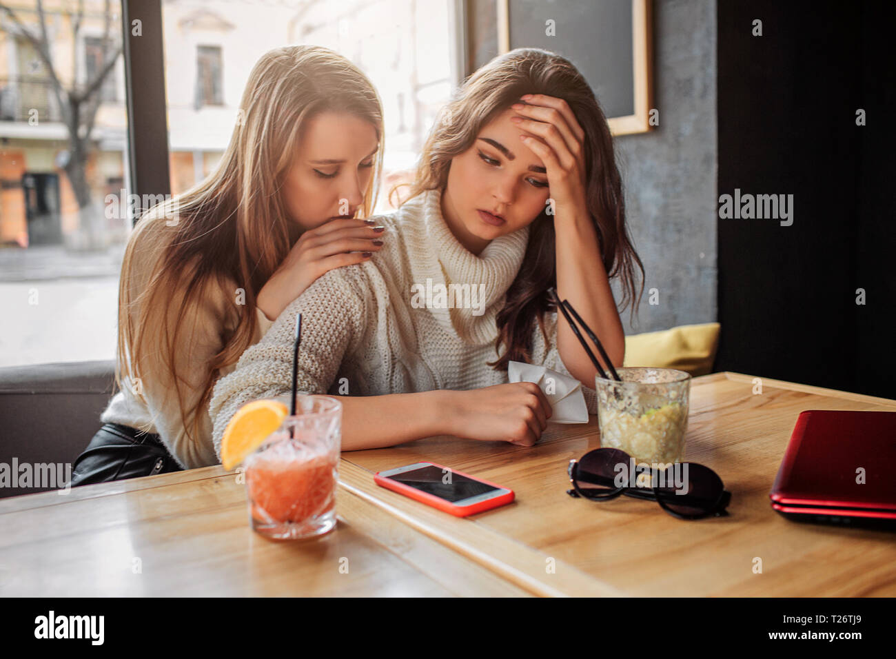 upset brunette lean on table and hold hand on forehead. Blonde woman ...